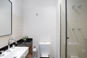 Casa de banho com lavatório branco, sanita e cabine de duche em vidro.