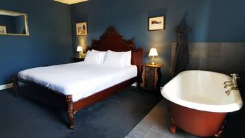 Quarto com uma cama grande, cabeceira de madeira, duas mesas de cabeceira com abajures e uma banheira grande de apoio.