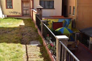 Um pátio com um pequeno jardim, uma cerca de metal e um mural colorido na parede.
