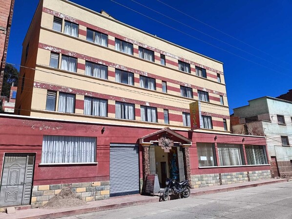 Edifício de vários andares com fachada vermelha e bege, apresentando entrada no térreo com uma motocicleta estacionada na frente.