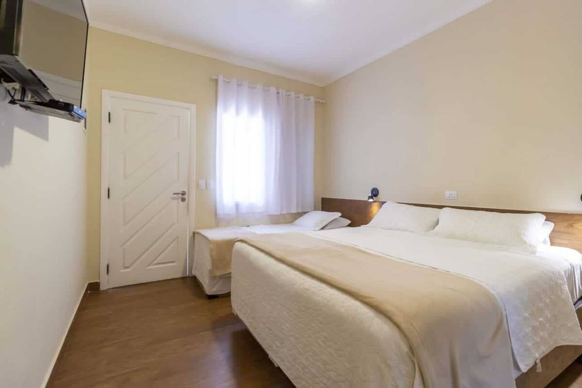 Quarto de hotel com duas camas, piso de madeira, porta branca e janela com cortinas.