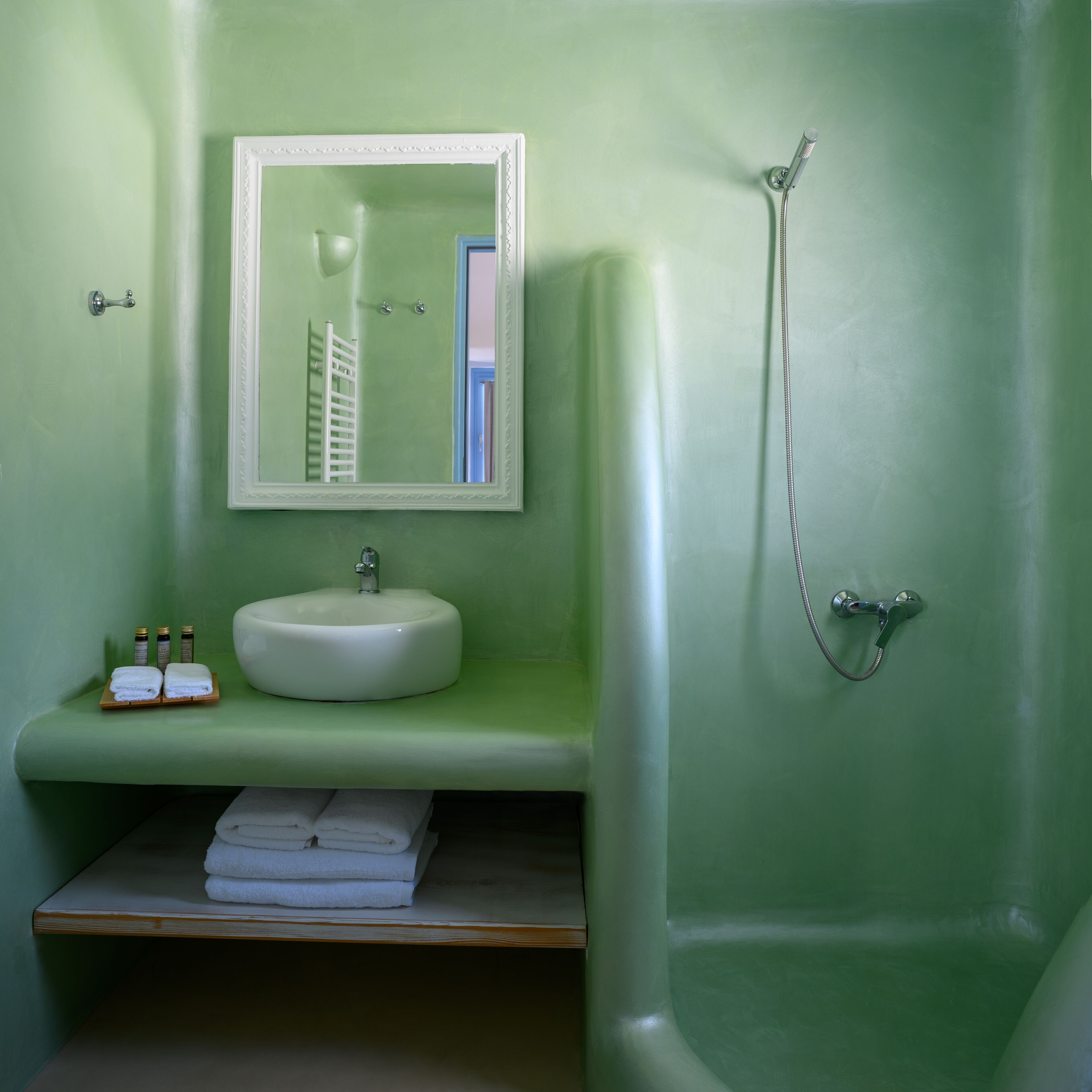 Um banheiro com parede verde, pia branca, espelho e chuveiro.