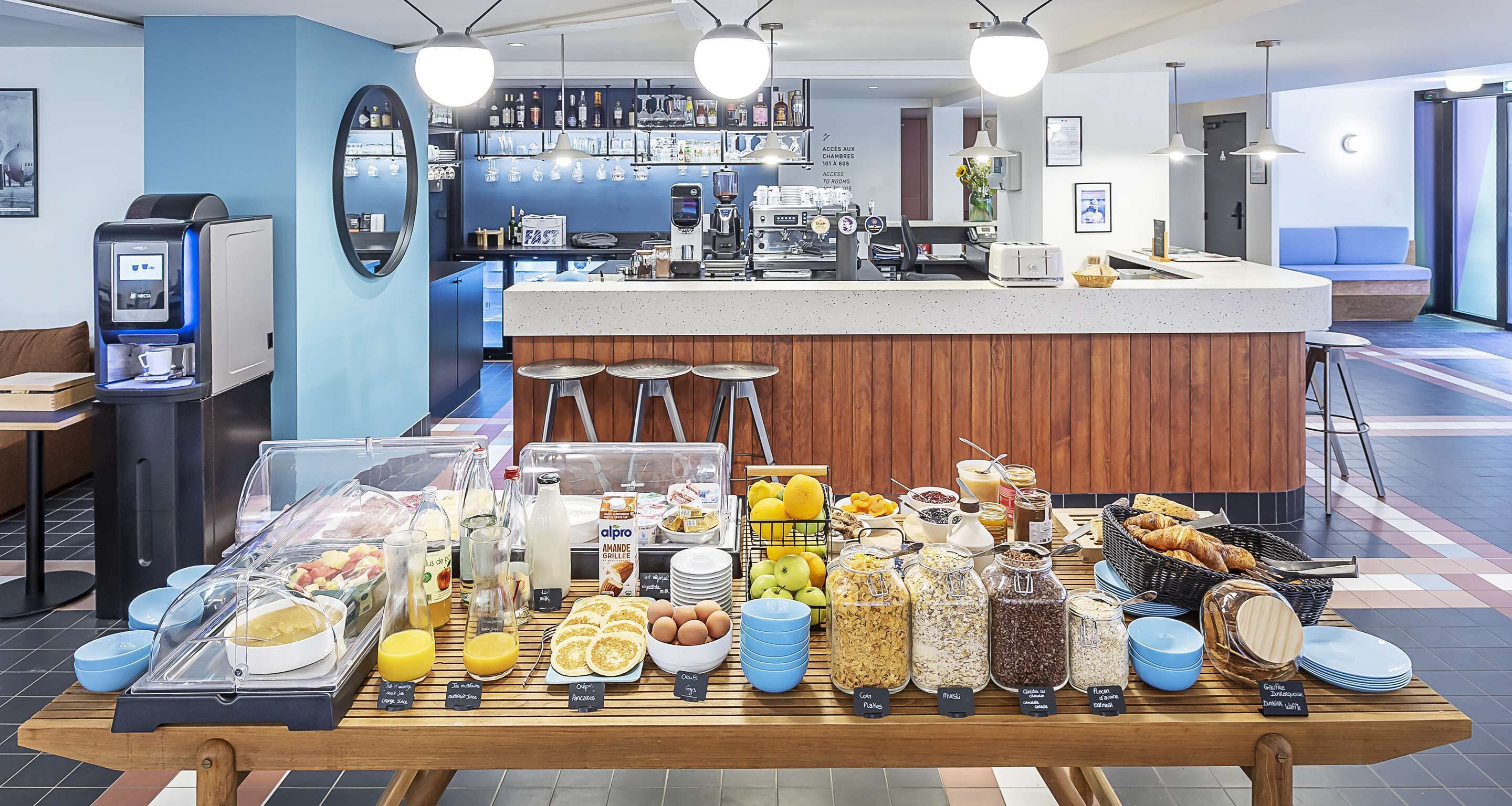 Um buffet de café da manhã com diversos alimentos e um espaço para café em um hotel moderno.