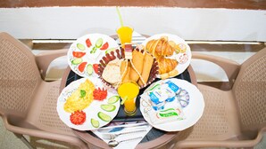 Mesa com itens de café da manhã, incluindo croissants, ovos e suco, em uma varanda com cadeiras.