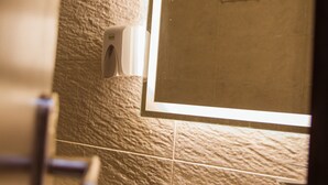 Casa de banho com lavatório branco, dispensador de sabonete líquido e espelho.
