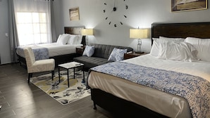 Quarto de hotel com duas camas, um sofá, uma mesa pequena e um relógio na parede.