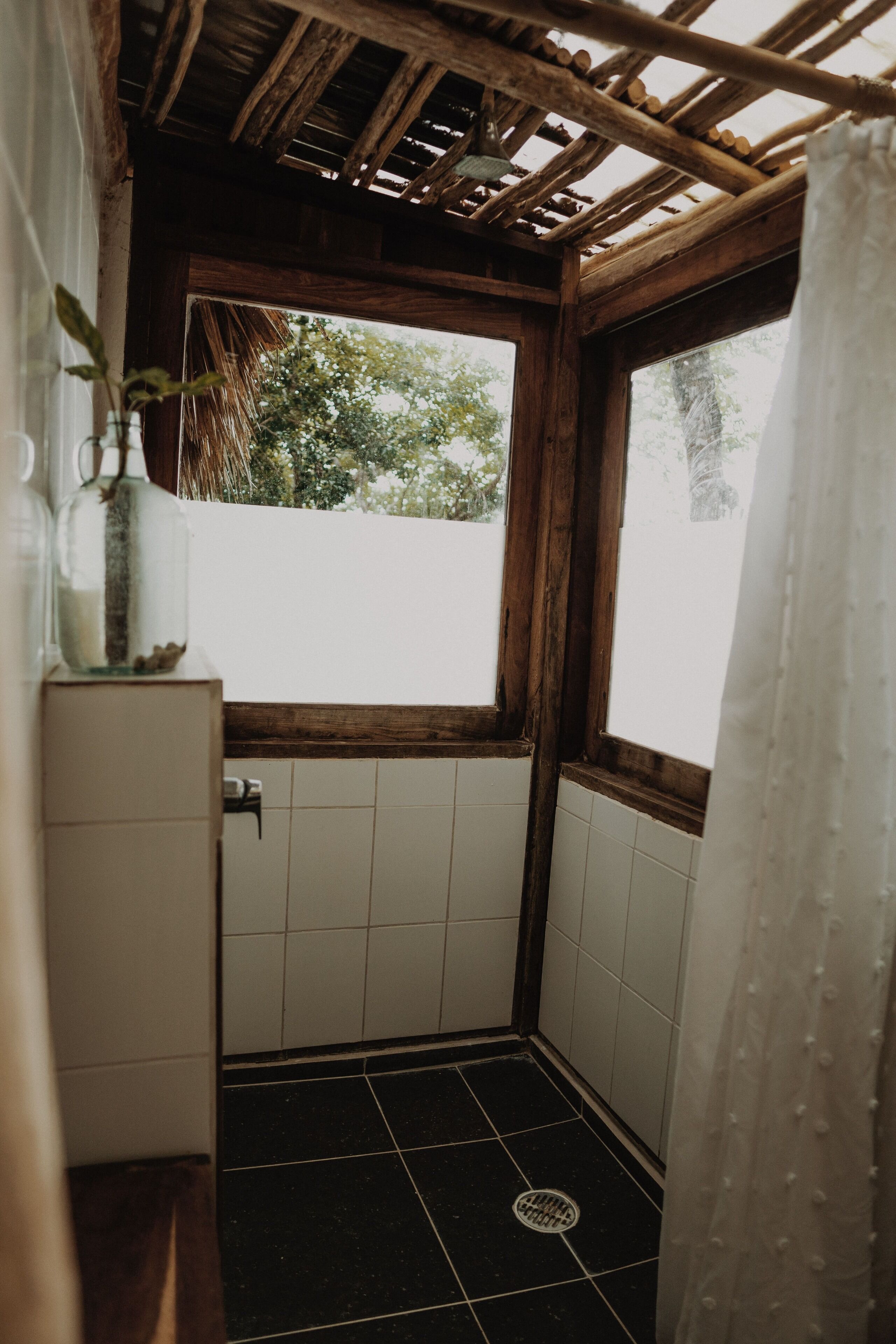 Uma casa de banho pequena e fechada, com teto de madeira, janela e chão em mosaico.