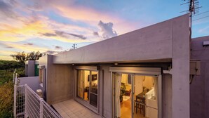 Um edifício residencial moderno com grandes portas de vidro deslizantes que dão acesso a uma sala de estar com sofá e mesa de jantar.
