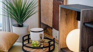 Um quarto com uma mesa de madeira redonda, uma planta em vaso, um abajur branco e uma estante de madeira.