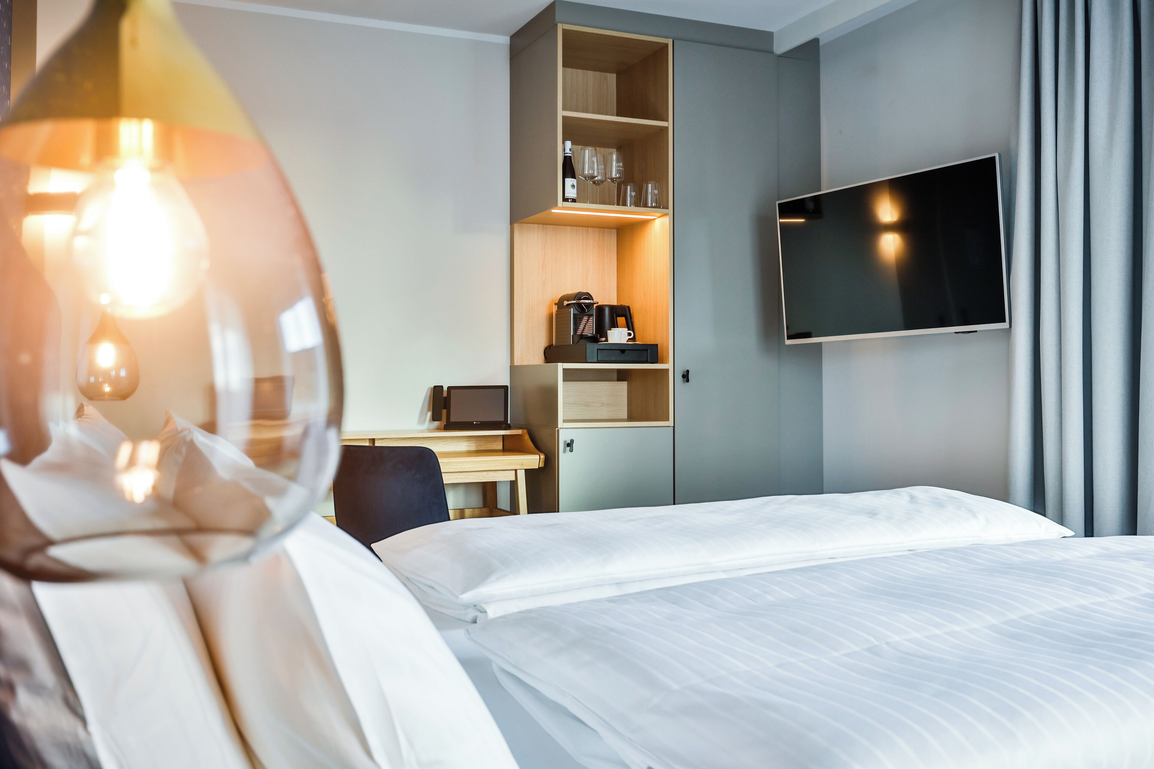 Quarto de hotel com cama, escrivaninha, televisão e minibar.