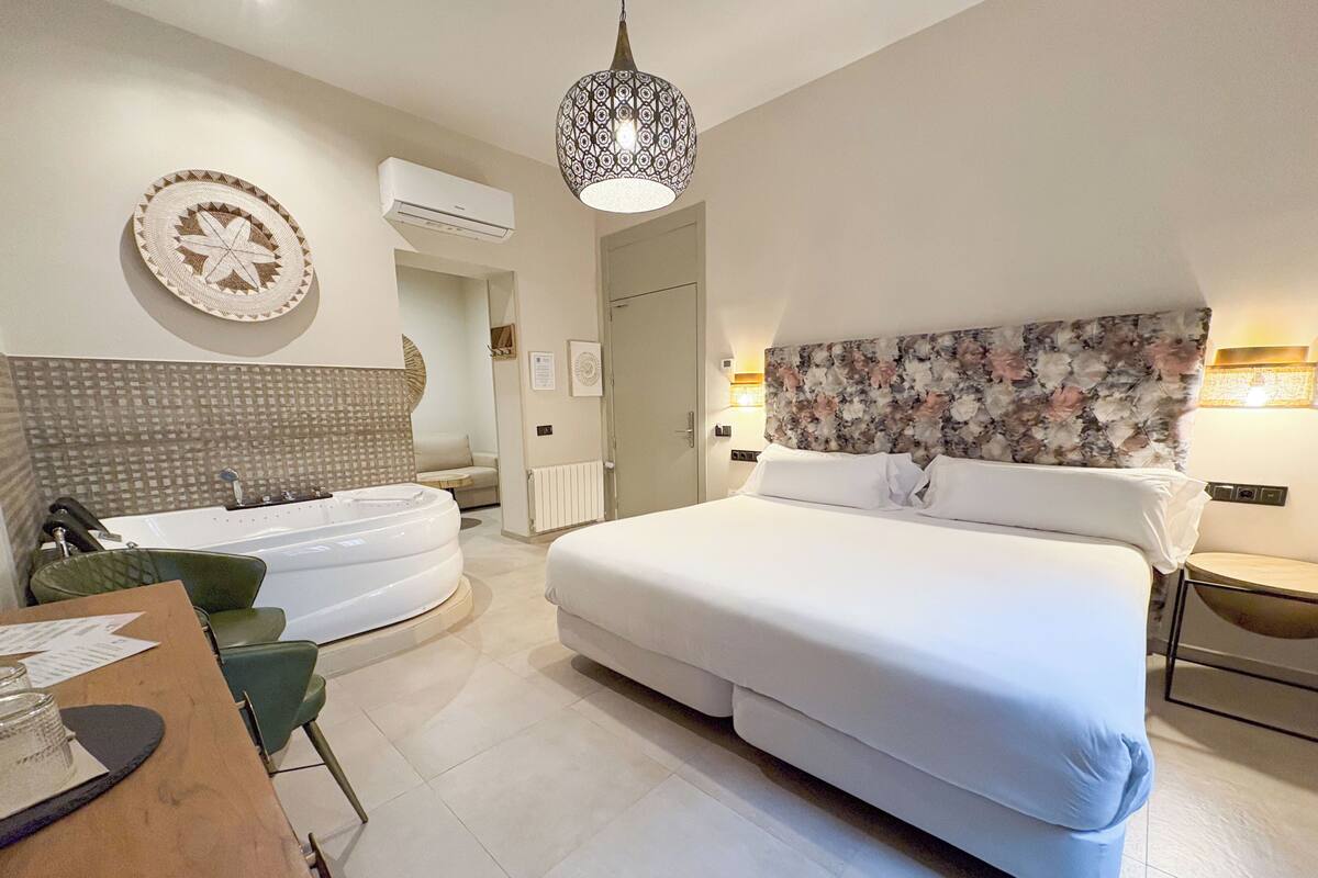 Quarto de hotel com uma cama grande, banheira, escrivaninha com cadeira e um objeto decorativo na parede.