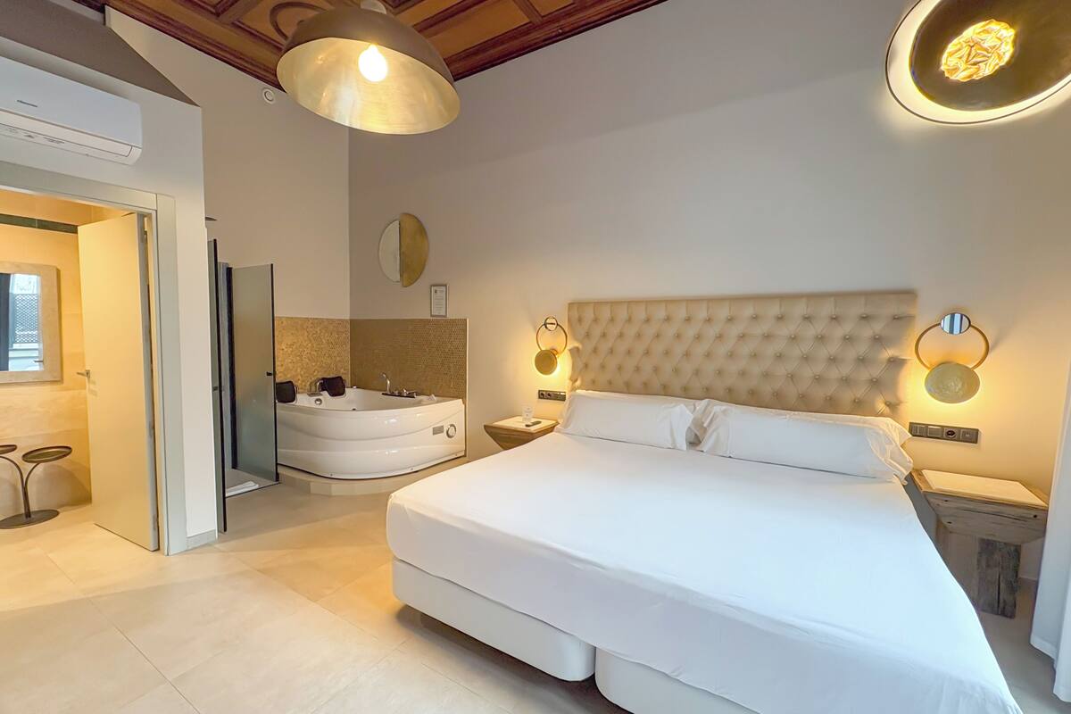 Quarto com uma cama grande, banheira integrada e luminária no teto.