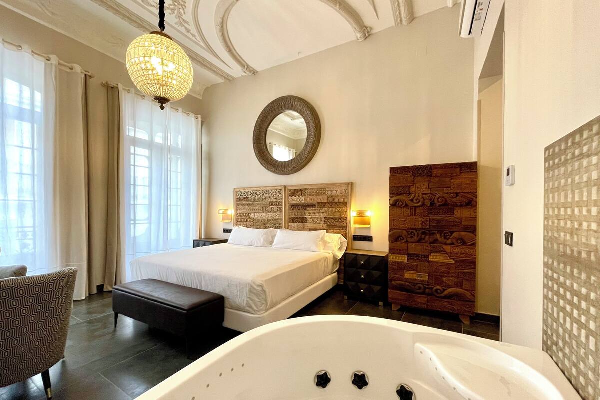 Um quarto espaçoso com uma cama grande, um espaço de estar, uma banheira e um espelho decorativo.