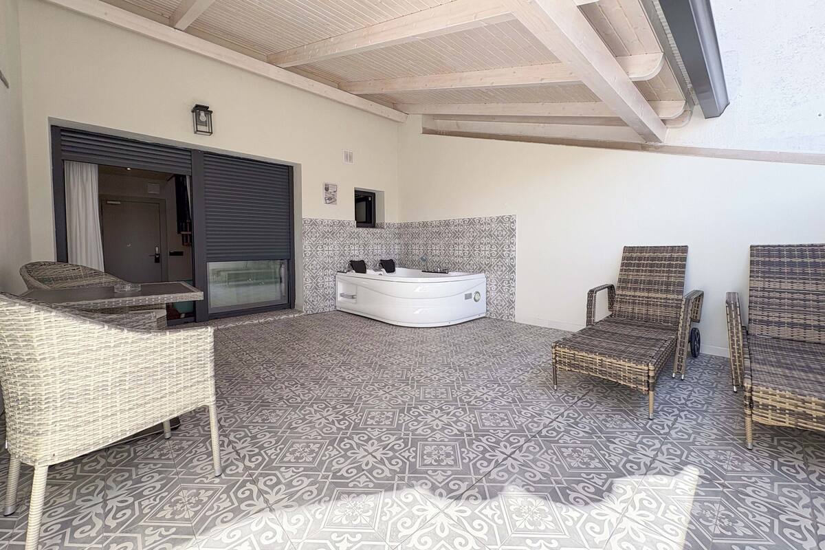 Um banheiro externo moderno com banheira separada, móveis de vime e piso de azulejos estampados.