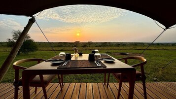 Mesa de jantar posta ao ar livre, com vista para o pôr do sol sobre uma paisagem gramada.