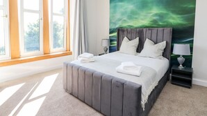 Quarto moderno com cama grande, vista do exterior pela janela e painel de parede verde.