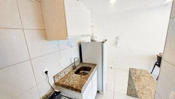 Uma cozinha compacta com paredes revestidas de azulejos brancos, bancada de granito, fogão a gás embutido e geladeira branca.