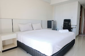 Quarto de hotel com uma cama grande, uma mesa de cabeceira, uma escrivaninha, uma cadeira, um espelho e um guarda-roupa.