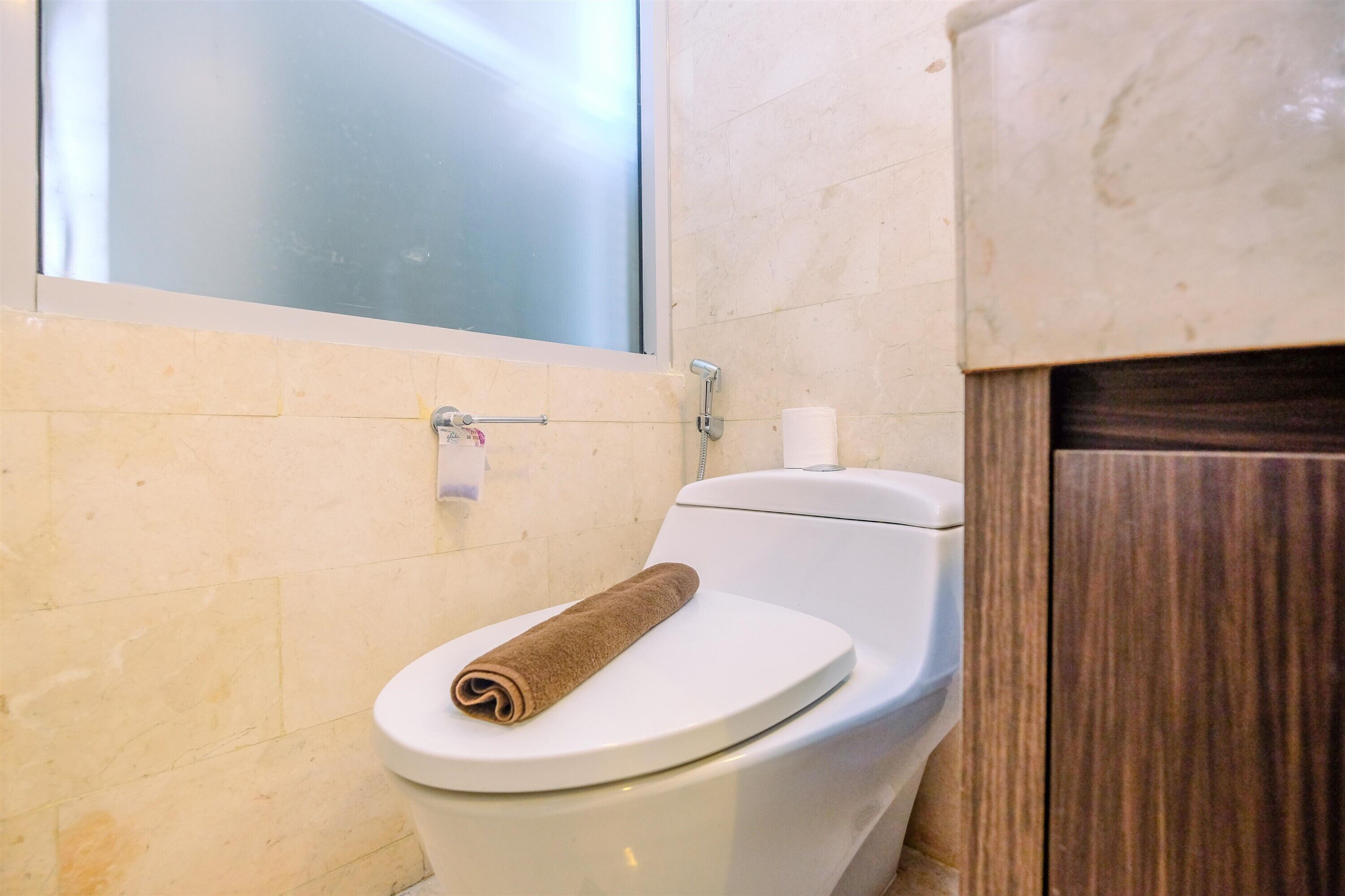 Casa de banho com sanita, toalha no assento, suporte para papel higiénico e janela.