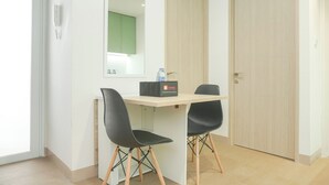 Um quarto pequeno com uma escrivaninha, duas cadeiras pretas, um espelho, um armário verde e uma porta de madeira.