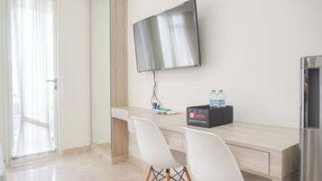 Quarto de hotel moderno com uma escrivaninha de madeira, duas cadeiras brancas, televisão de tela plana na parede, minibar e uma porta com cortina translúcida.