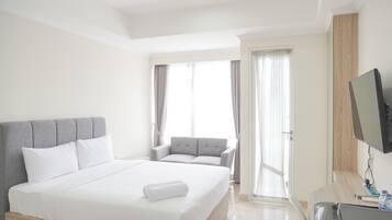 Quarto de hotel com uma cama grande, um sofá cinza estofado, uma televisão e uma janela com cortinas.