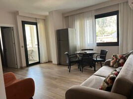 Uma sala de estar moderna com sofá, mesa de jantar e cadeiras, geladeira e porta de vidro deslizante para uma área externa.