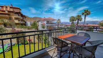 Uma varanda com mesa e cadeiras, com vista para uma área residencial com casas e montanhas.
