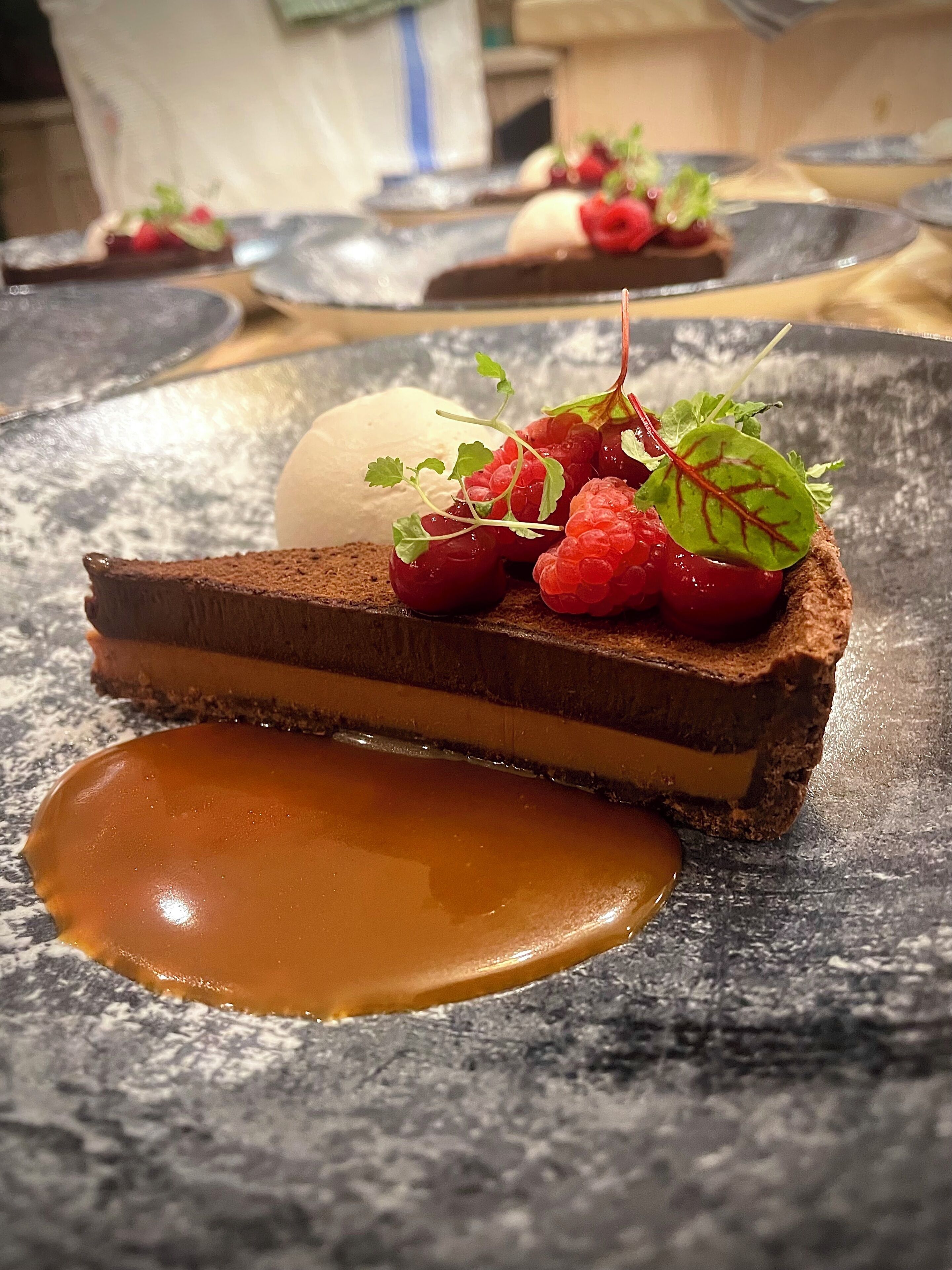 Uma sobremesa com base de chocolate, framboesas e uma bola de sorvete sobre um prato de ardósia.