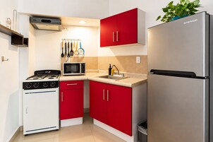 Cozinha compacta com fogão a gás, micro-ondas, pia e geladeira de aço inoxidável.