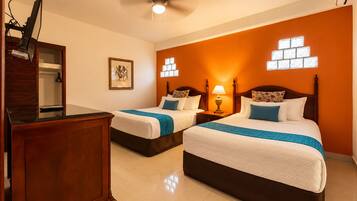 Quarto de hotel com duas camas, cómoda de madeira, ventoinha no teto e luminária fixada na parede.
