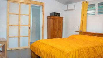 Quarto com cama, guarda-roupa de madeira, mesa pequena, televisão e janela com cortinas.