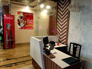 Um espaço de escritório com uma mesa de recepção, máquina de venda automática de Coca-Cola e um cartaz promocional para um prato especial tailandês.