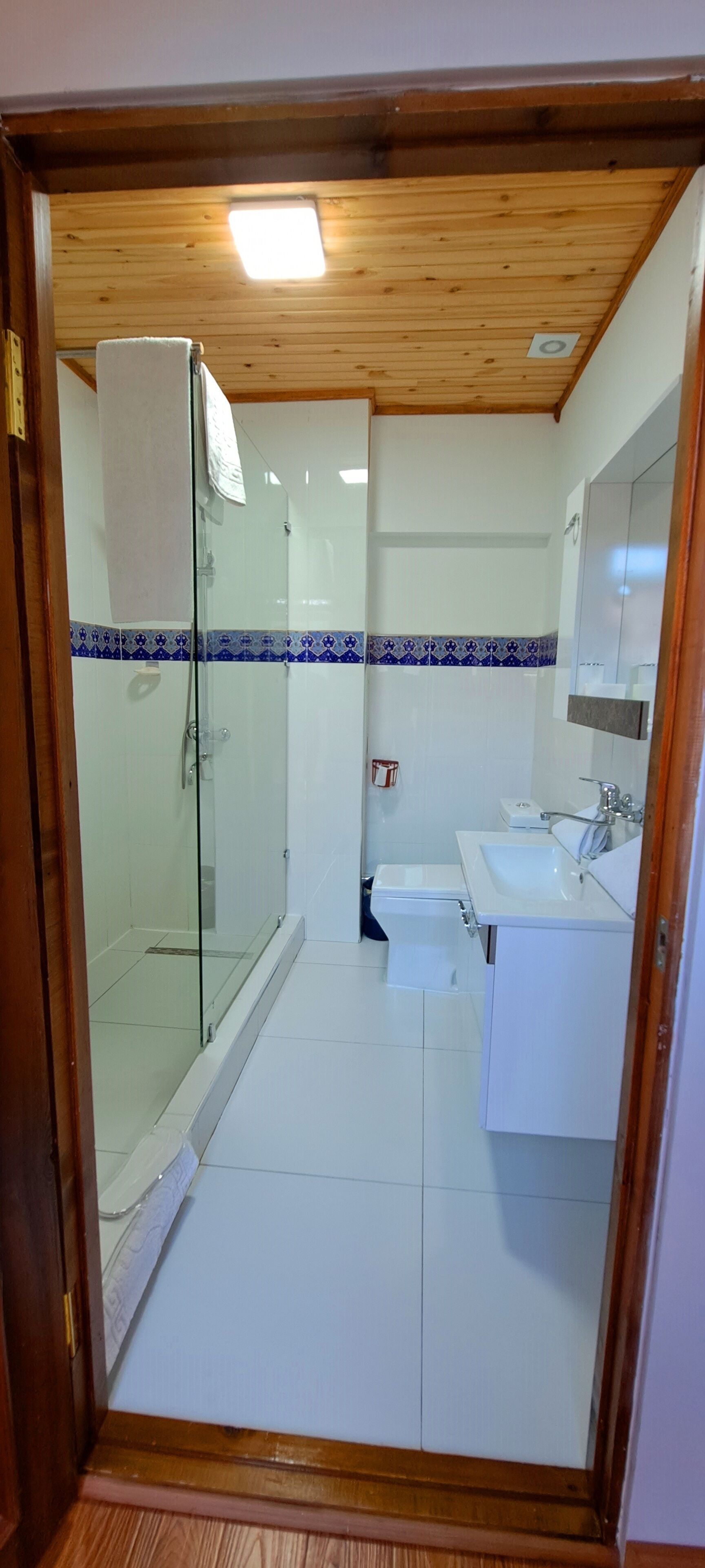 Uma casa de banho com cabine de chuveiro em vidro, uma pia branca e um espelho.