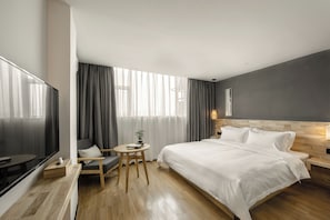 Quarto de hotel moderno com uma cama grande, televisão, escrivaninha e uma cadeira.