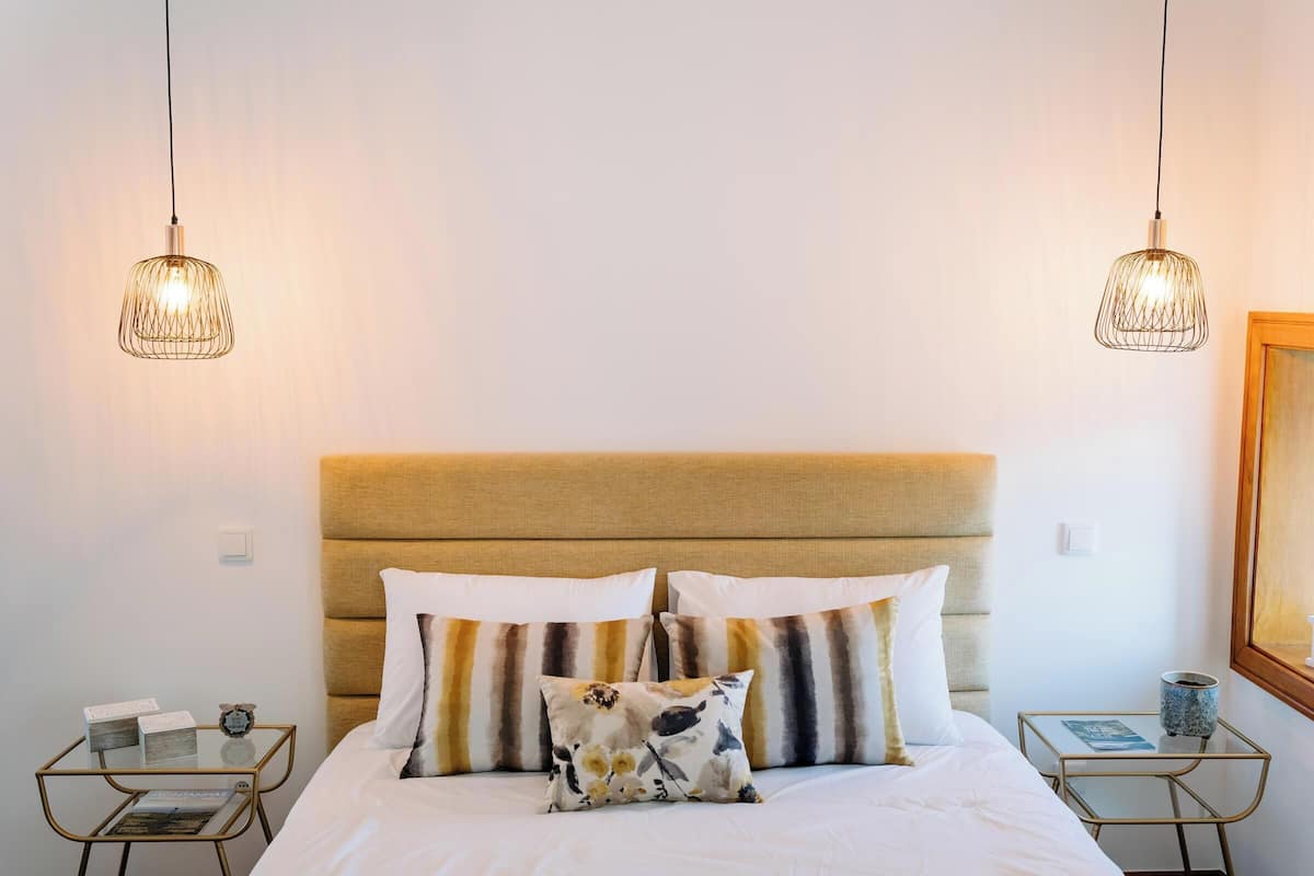 Cama bem arrumada com cabeceira, duas mesas de cabeceira e duas luminárias pendentes.