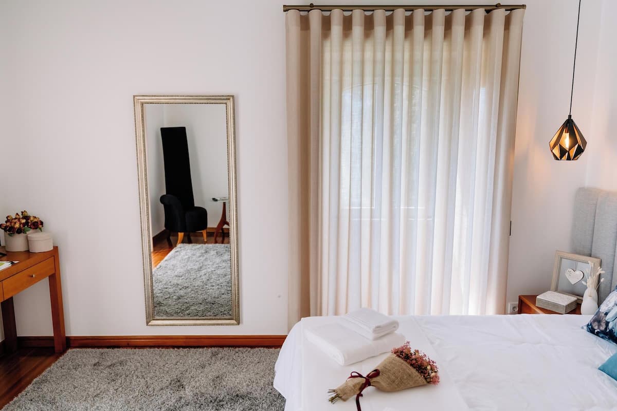 Quarto de hotel com cama, espelho, escrivaninha, cadeira e janela com cortinas.