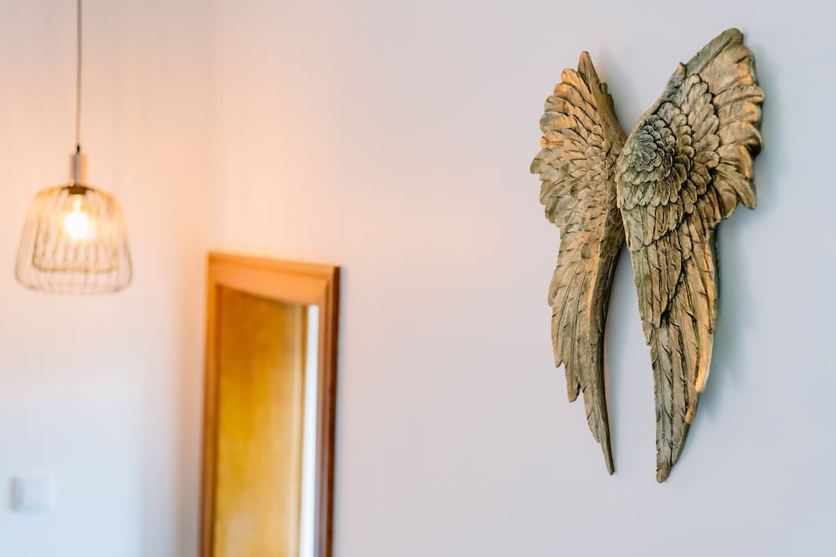 Uma peça decorativa na parede com formato de asas, um lustre pendente e um espelho emoldurado.