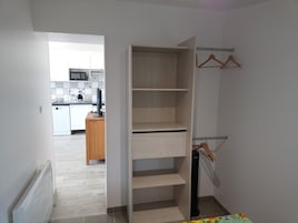 Quarto com guarda-roupa de madeira, radiador e cozinha ao fundo.