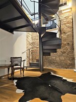 Um interior moderno com escada em espiral, paredes de pedra, mesa de jantar de madeira e tapete de couro de vaca em preto e branco.