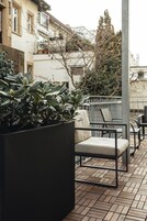 Terraço com mesas ao ar livre, plantas em vasos e vista para edifícios.
