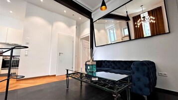 Uma sala de estar moderna com um sofá azul escuro, uma mesa de centro de vidro e um espelho grande na parede.