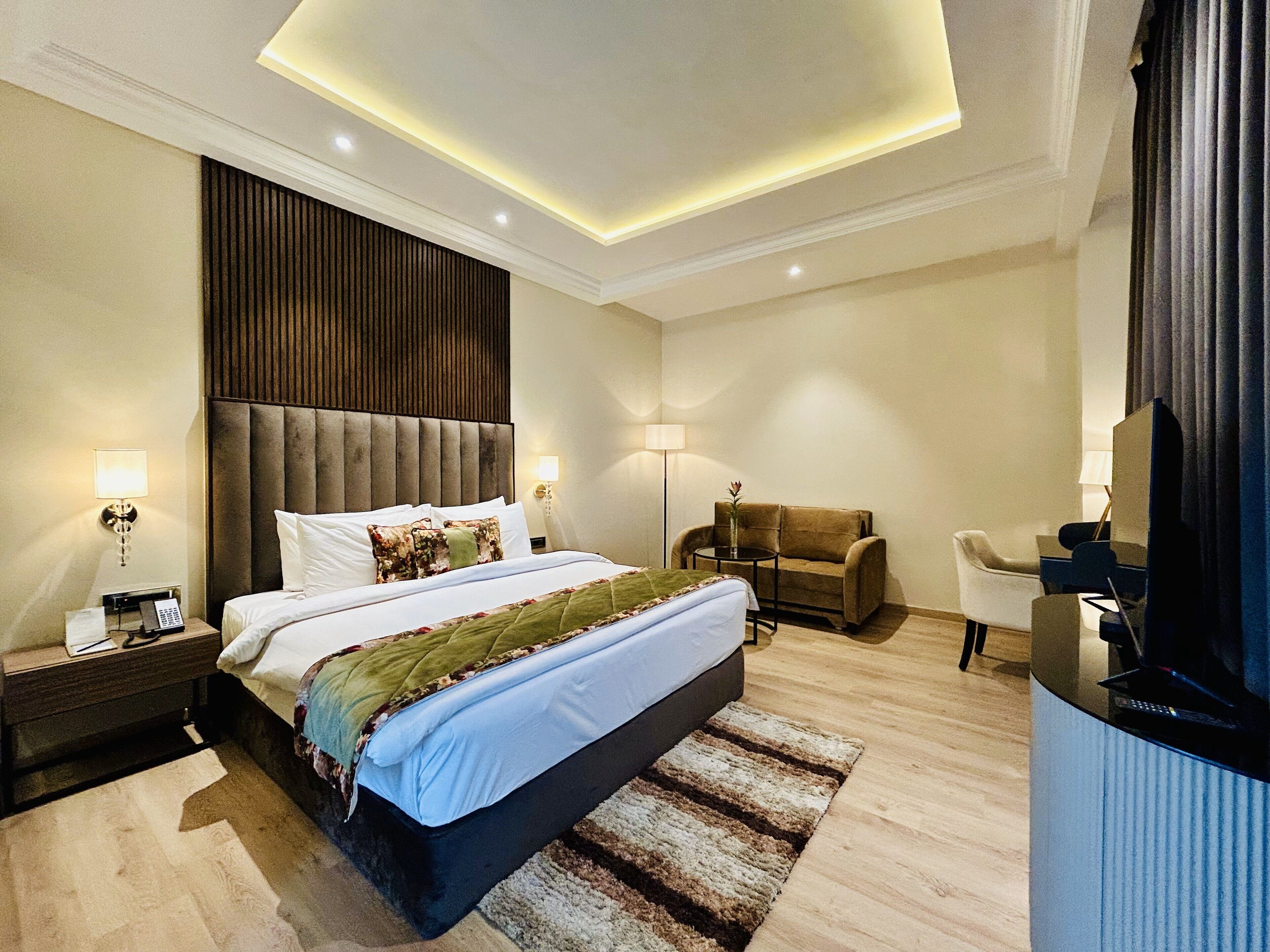 Quarto de hotel moderno com uma cama grande, um sofá, uma escrivaninha e uma televisão.
