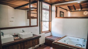 Casa de banho com soalho de madeira, duas pias, uma banheira e uma janela com persianas.