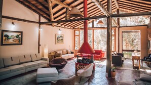 Uma sala de estar ampla com teto de madeira alto, lareira e janelas grandes que oferecem vista para o exterior.