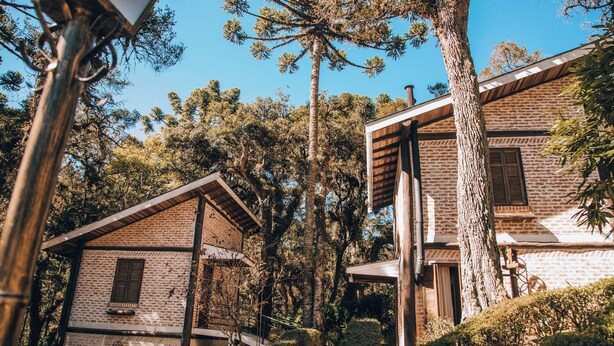 Um edifício rústico com fachada de tijolos, vigas de madeira e um caminho rodeado de árvores.