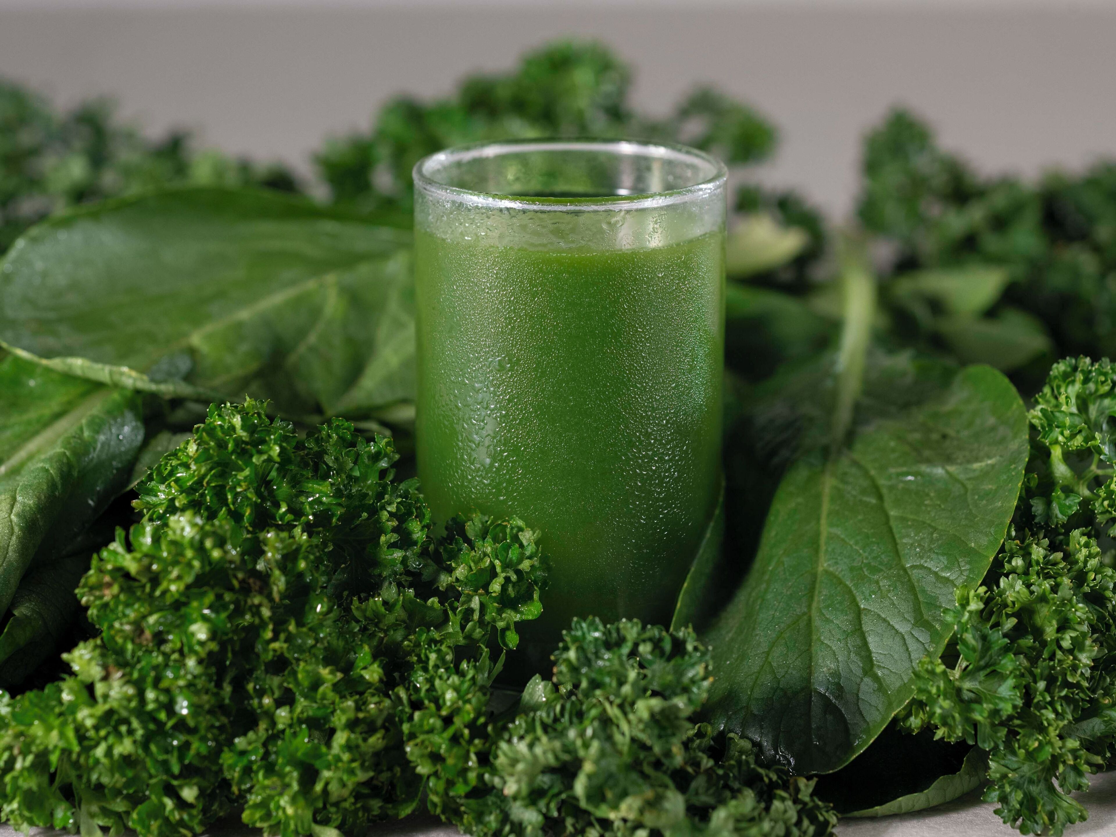 Um copo de suco verde envolto em folhas frescas de couve.
