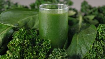 Um copo de suco verde envolto em folhas frescas de couve.