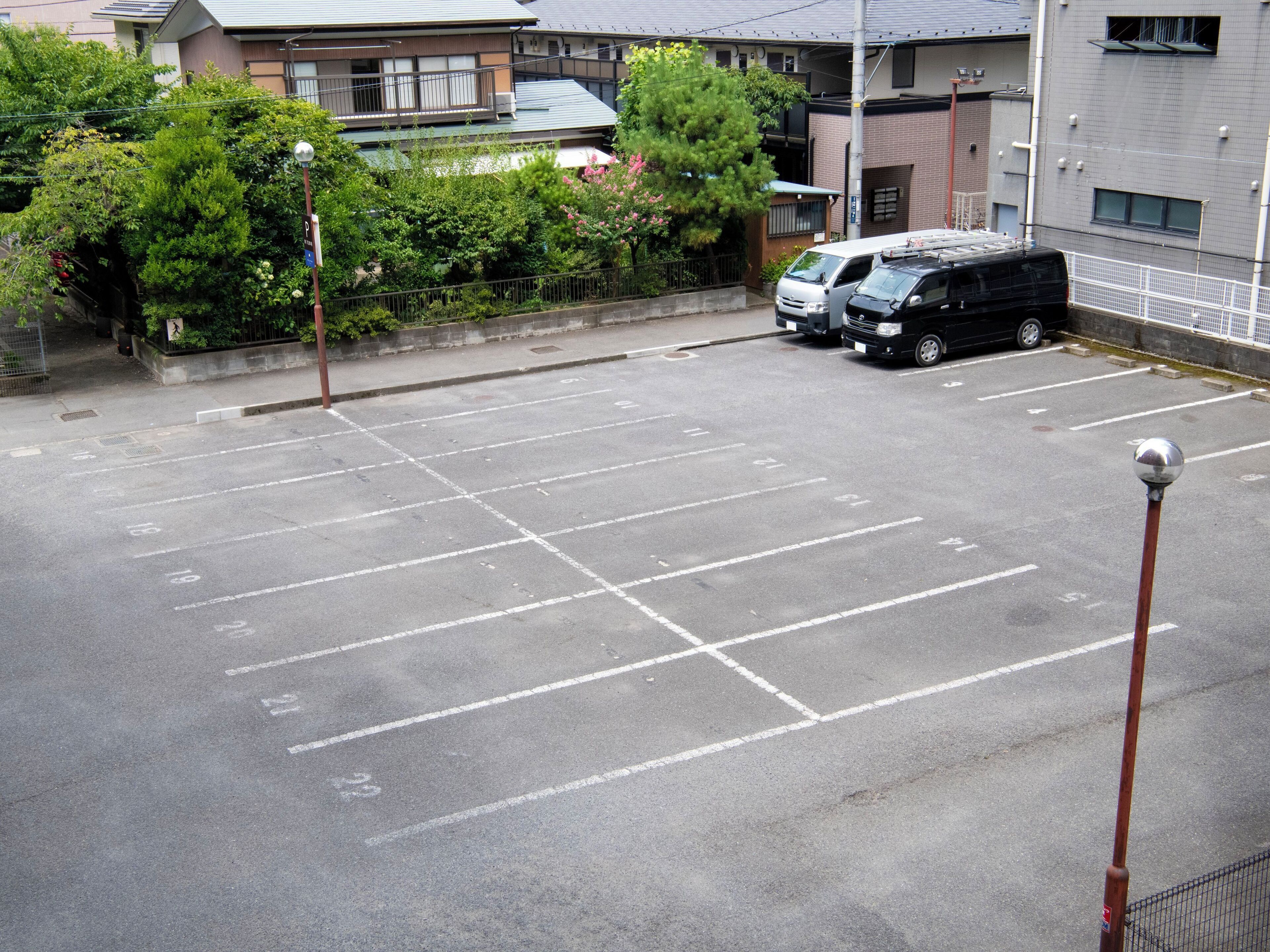 Um estacionamento com vagas demarcadas, uma van preta e um edifício ao fundo.
