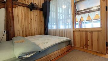Quarto de cabana de madeira com cama, ventilador e janela com cortinas.